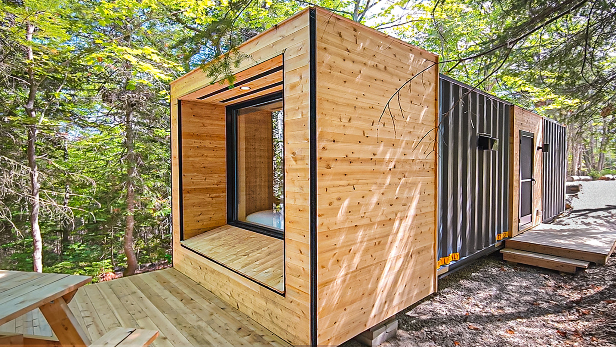 Une mini maison container bardée de bois avec des grandes baies vitrées